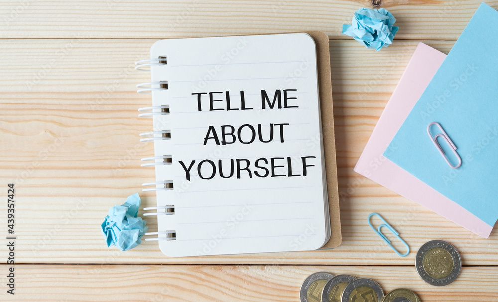On a white background lies a notebook with words TELL ME ABOUT YOURSELF ...