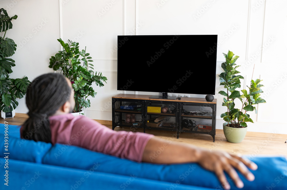 Relaxed African-American man with locks watching TV at home, back view ...