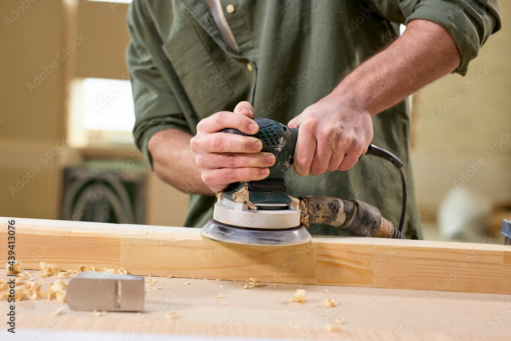 Cropped male carpenter carefully smoothing wooden material with ...