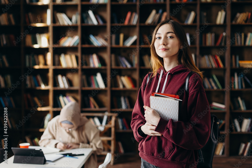 Content female student standing with books in library Stock Photo ...