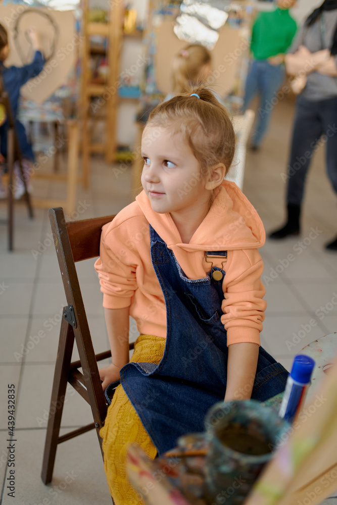 girl in uniform at a drawing class, drawing with paints at an easel ...