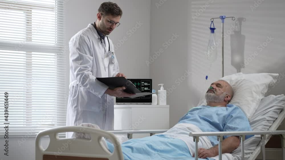 Young doctor talking to senior man resting in hospital bed. Male RN ...