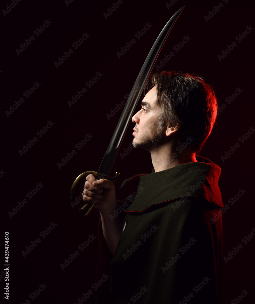 Portrait of strong adult man warrior in cape standing sideways holding ...