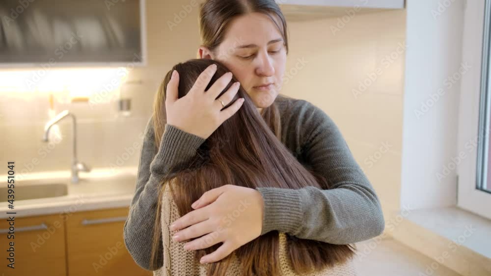 Young mother hugging and consoling upset crying daughter on kitchen. Parent supporting and ...
