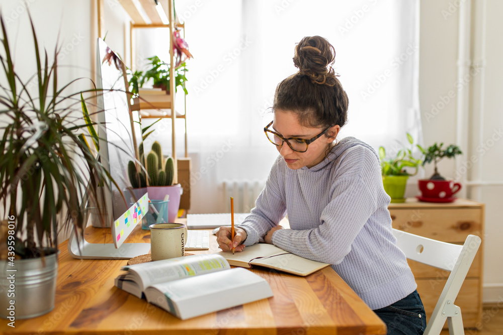 Young woman studying at home, she attends an online class and writes ...