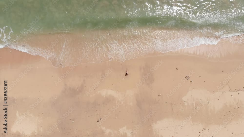 Top-down view of empty beach, one woman in bikini lying on sand. Aerial ...
