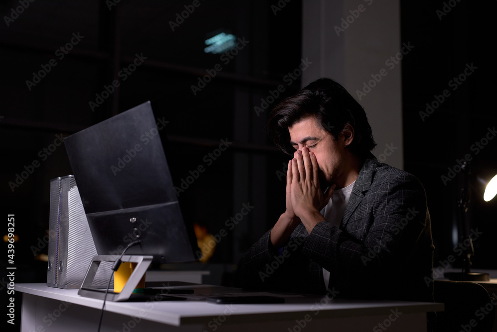 Portrait of tired male in suit sitting at desk in office using computer ...