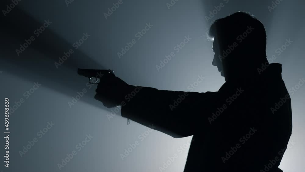 Silhouette male shooter aiming pistol in darkness. Criminal man raising ...