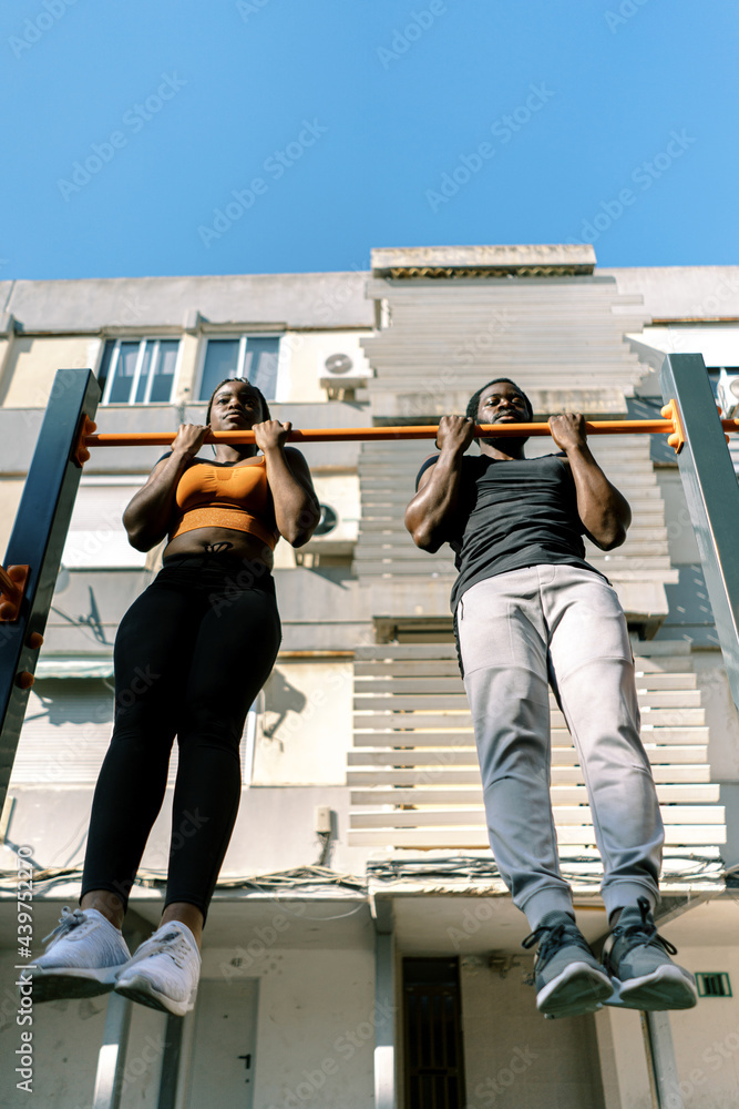 Sporty couple doing pull ups on sports ground Stock Photo | Adobe Stock