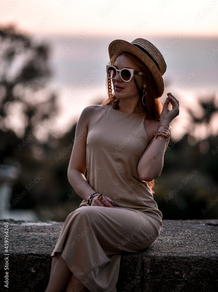 Gorgeous wealthy redhead woman at summer sunset sitting on stone ...