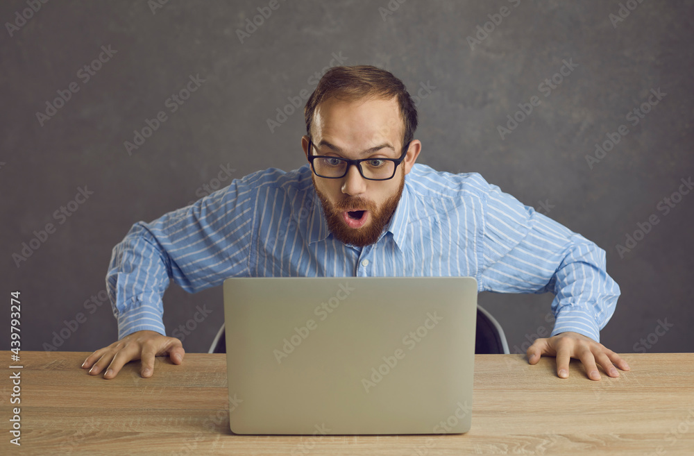 Funny open mouthed nerd in eyeglasses looking at laptop computer screen ...