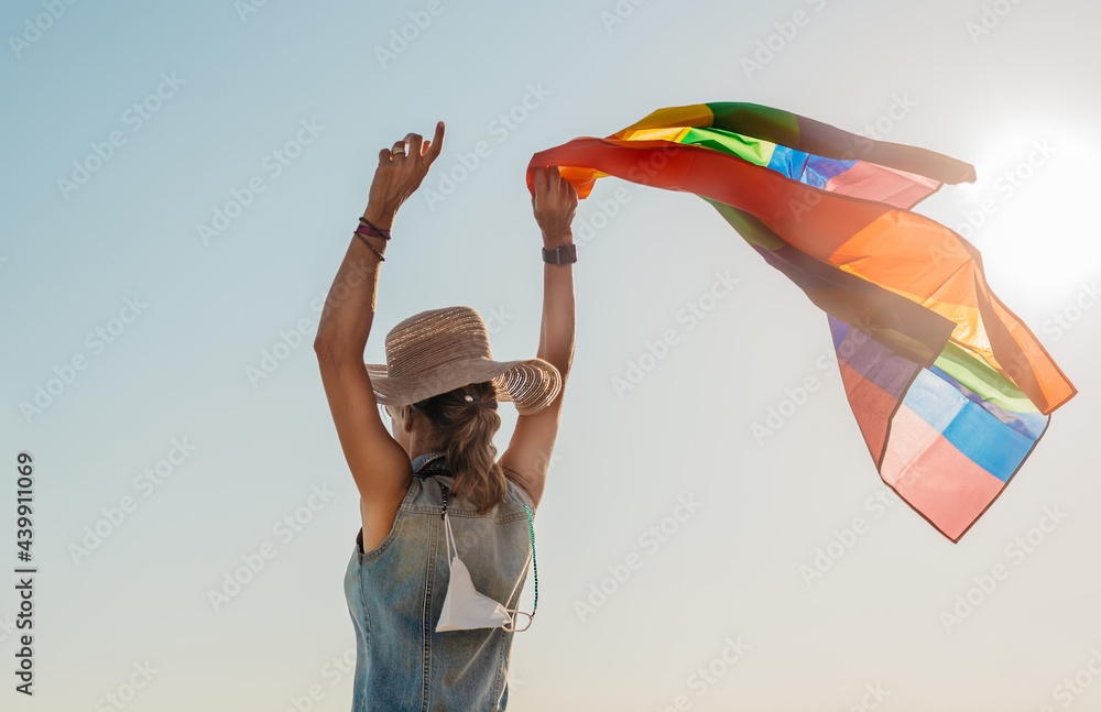 a woman raises her arms with a pride flag in her hand. she is ...