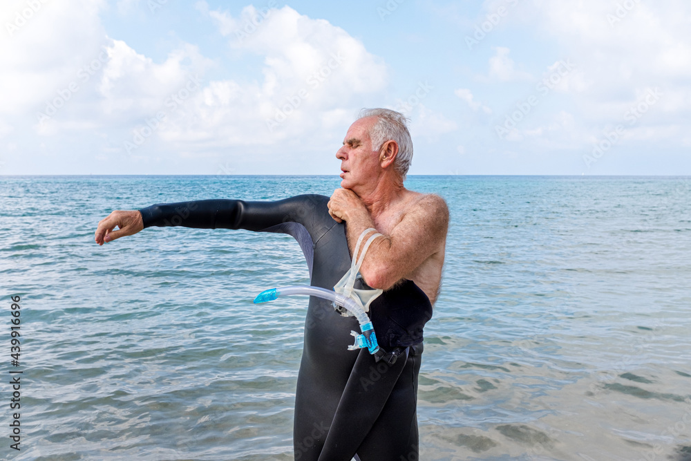 Older retired man putting on his wetsuit on the beach to go swimming ...