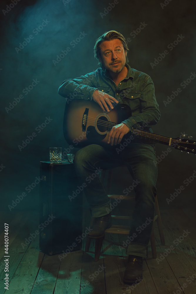 Musician sitting on a wooden stool with an acoustic guitar with next to ...