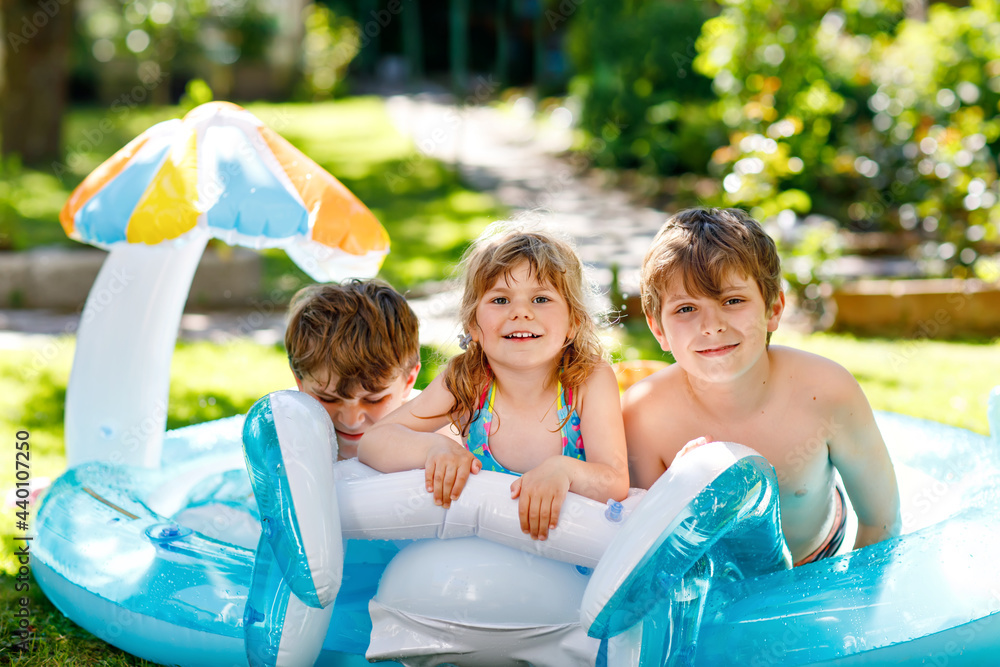 Three kids, two boys and toddler girl splash in an outdoors swimming ...
