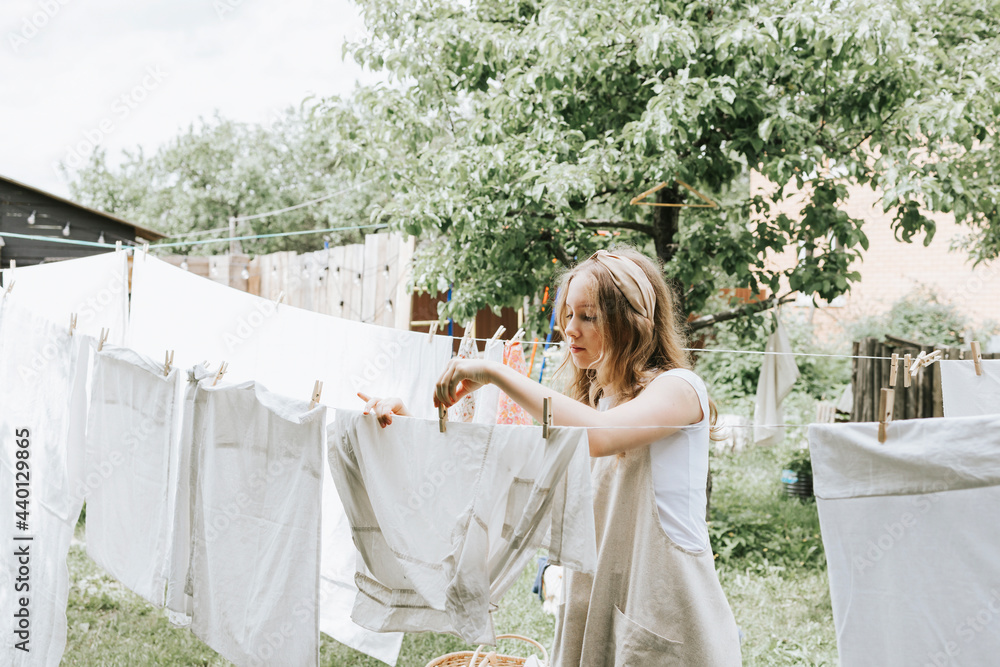 blonde teen girl in linen apron is doing homework washing clothes in ...