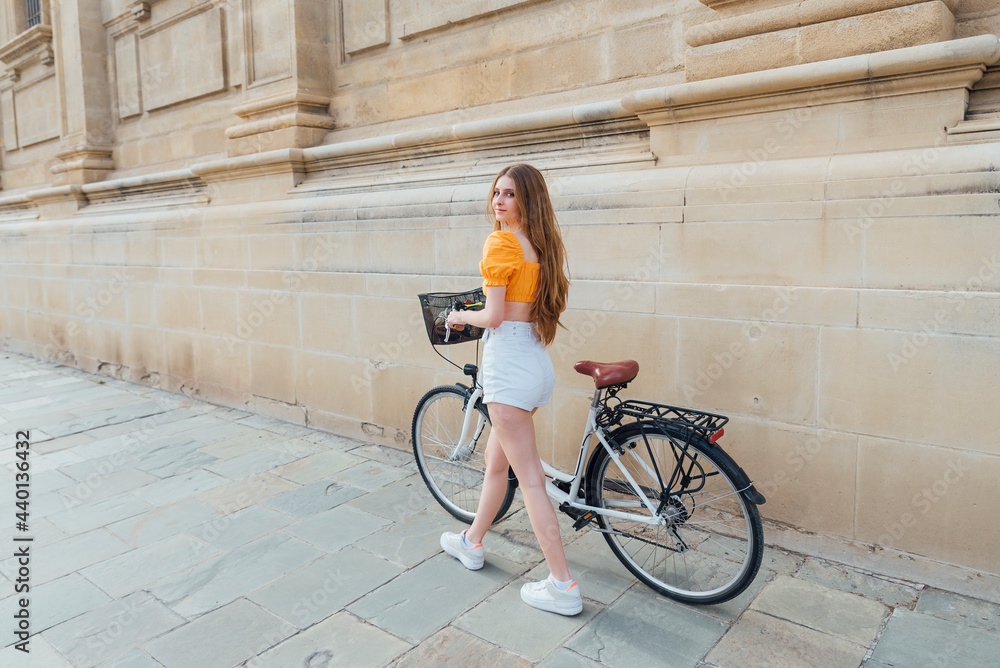 Young woman looking away while wheeling bicycle by stone wall Stock 写真 ...