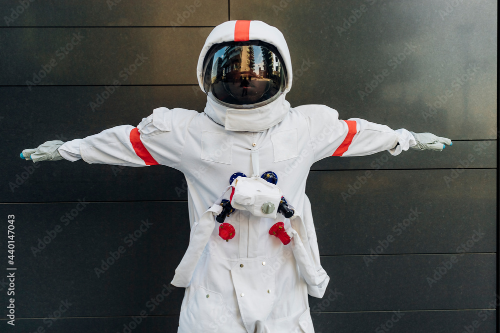 Male astronaut with arms outstretched wearing space helmet standing by ...