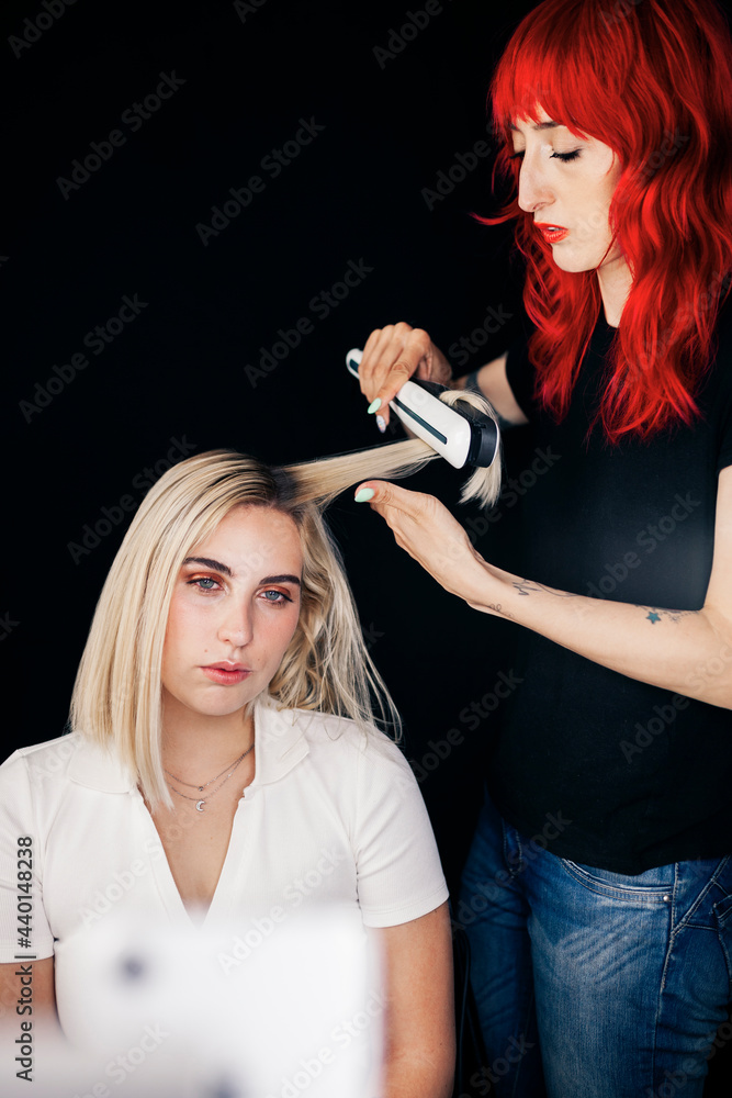 Female blogger recording while doing straightening on model's hair at ...