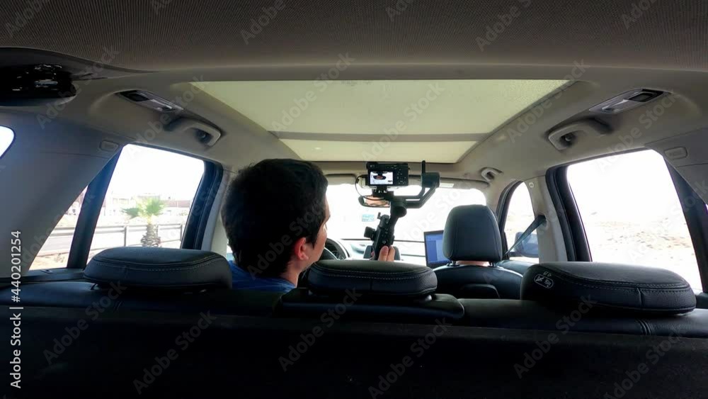 view inside a car from behind of a man filming his friends on a road ...