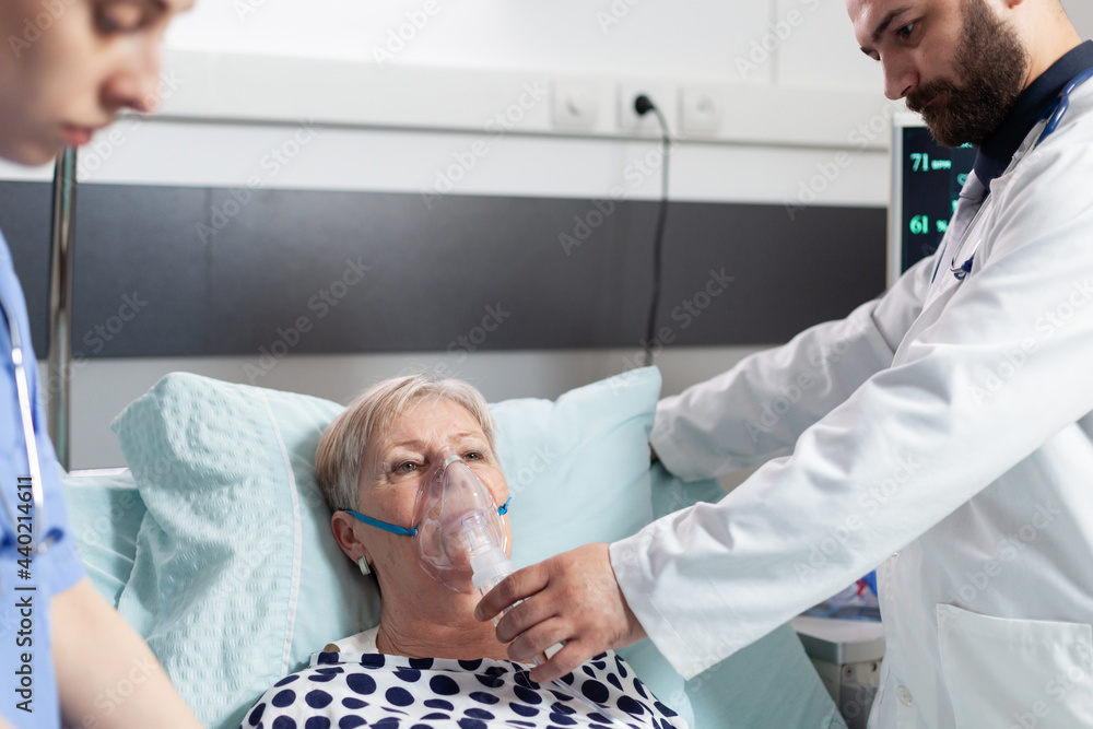 Doctor and nurse supervising senior woman breathing with oxygen mask ...