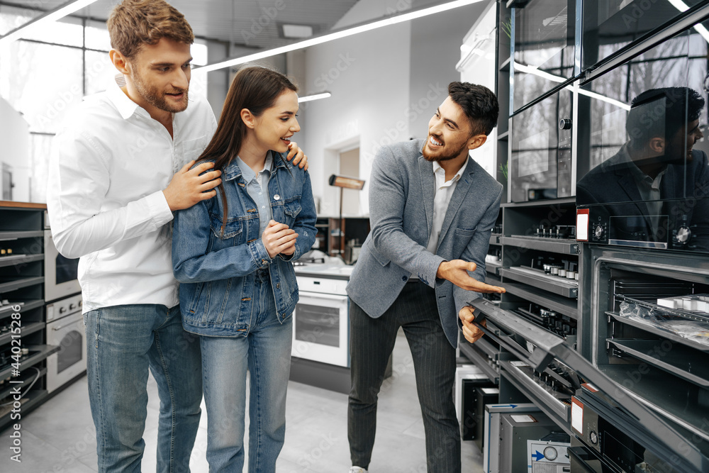 Male shop assistant helps young couple to choose new home appliance ...