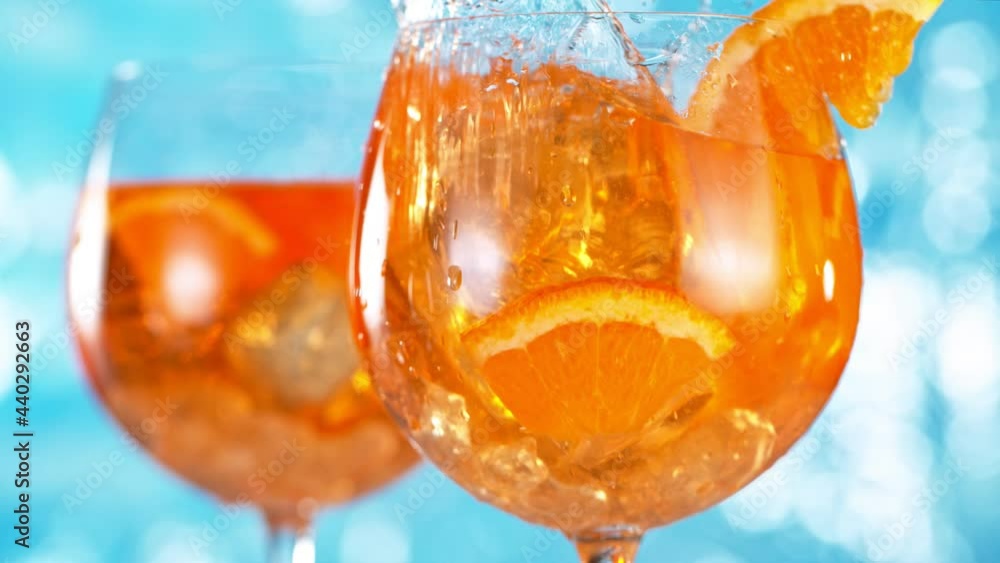 Super slow motion. Ice cube falling into glass of orange cocktail ...
