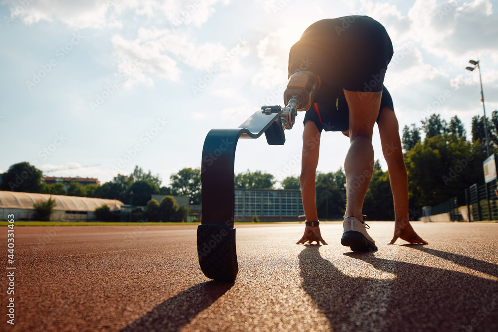 Rear view of runner with prosthetic leg at starting line on running ...