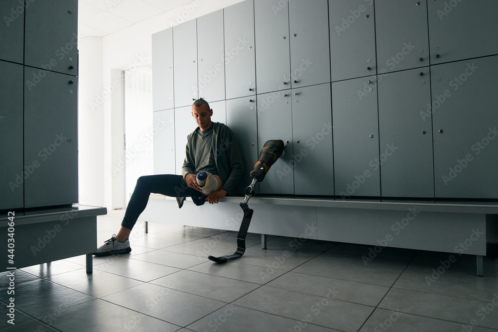 Athletic amputee putting on prosthetic leg in locker room and preparing ...