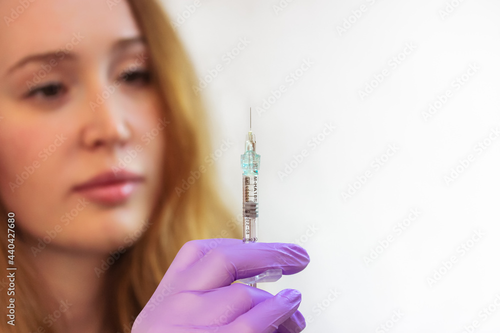 A young woman doctor wearing purple rubber gloves holds an injection ...
