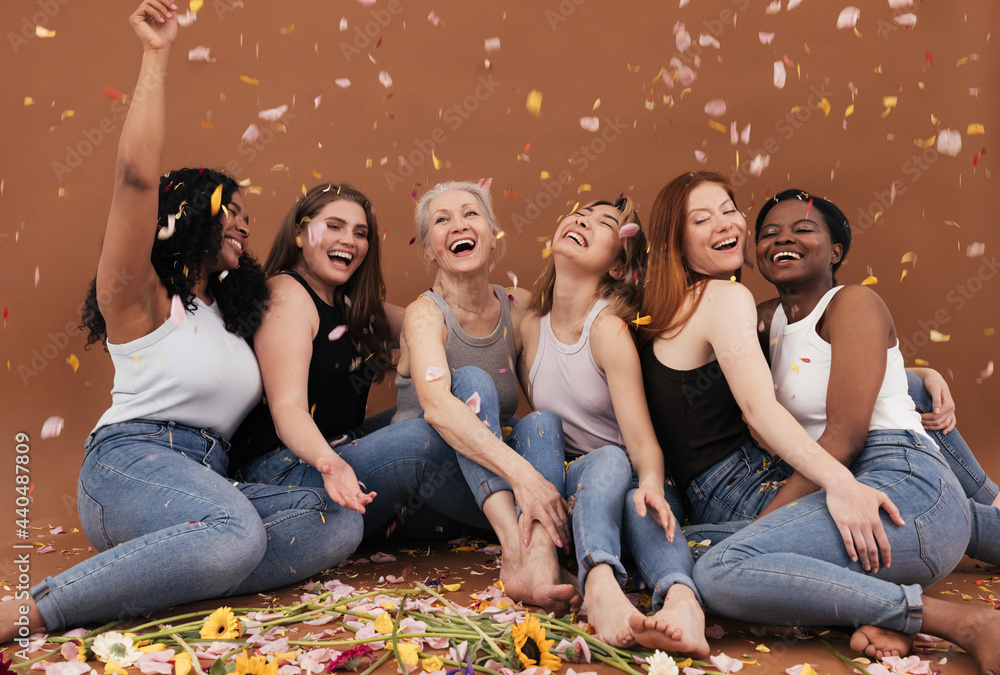 Group of happy women sitting on the brown background while petals from ...