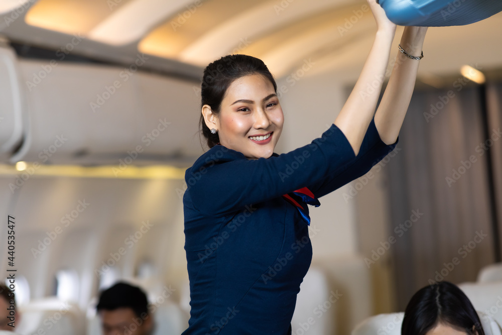 flight attendant helping passenger put luggage to cabin or compartment ...