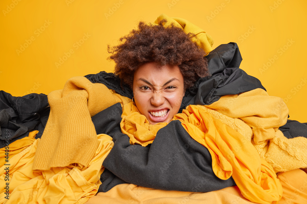 Curly haired young woman sticks out head from pile of clothes smirks ...