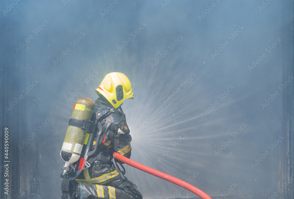A firefighter or fireman with uniform using water fire hose against hot ...