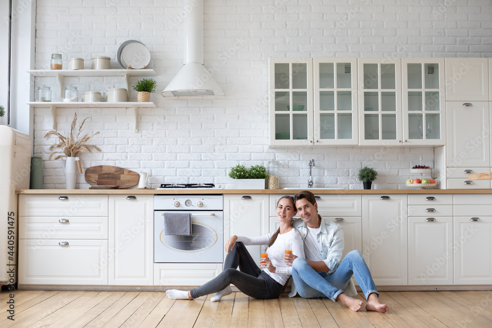 Smiling couple young guy and girl sit on warm kitchen floor talking ...