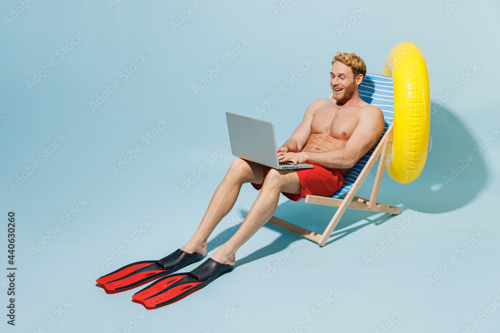 Full length young freelancer man in red shorts swimsuit sit in ...