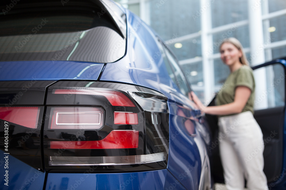 Selective focus on car lights, woman examining car at auto dealership ...
