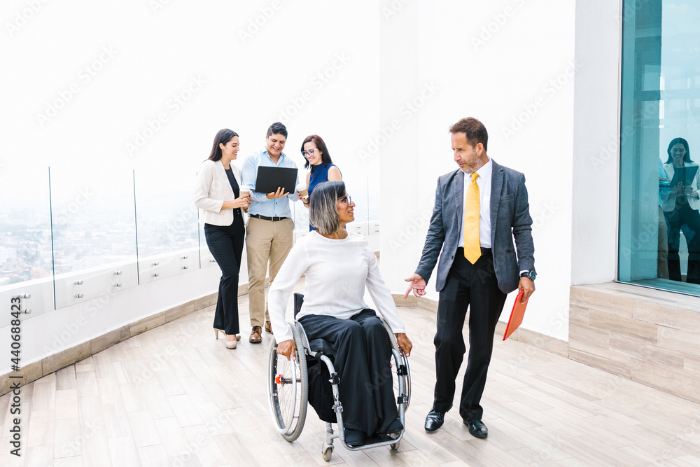 Smiling Hispanic transgender woman in wheelchair and coworker ...