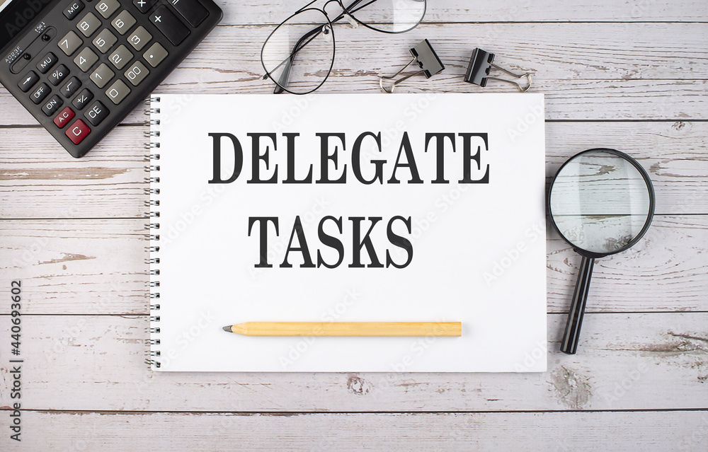 Blank notebook with text DELEGATE TASKS on the white background with ...