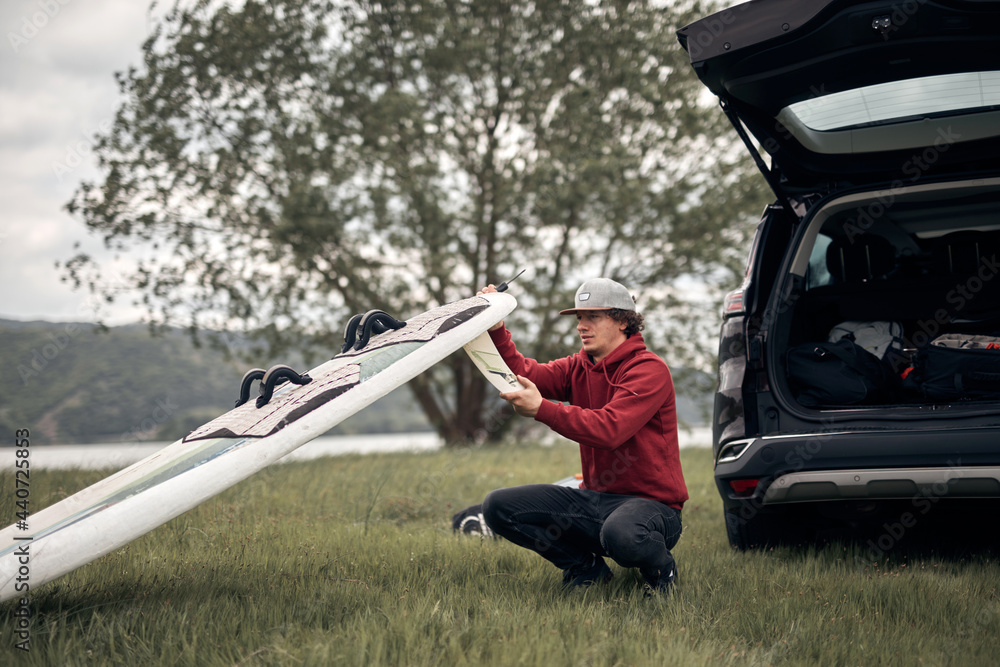 Windsurfer and camper packing and unpacking from a car's roof rack in ...