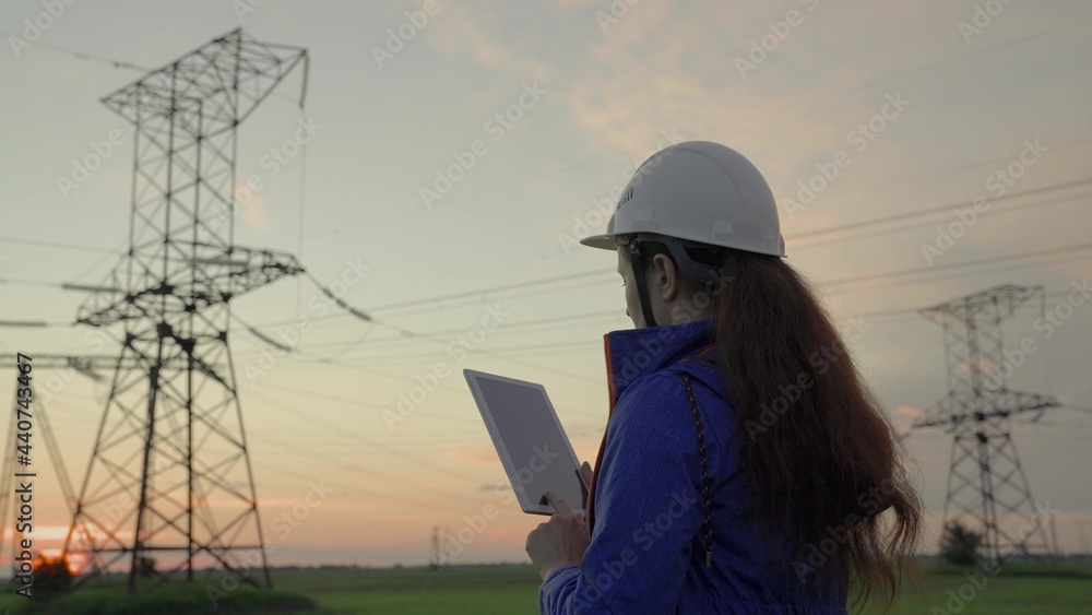 Woman power engineer in a white helmet checks power line using data ...