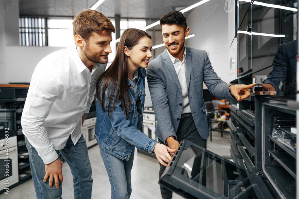 Male shop assistant helps young couple to choose new home appliance ...