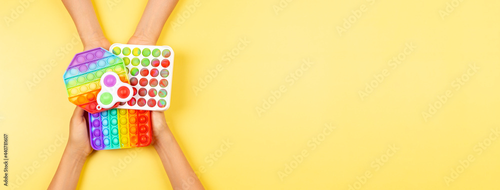 Hands holding colorful pop it fidget toys on yellow background. Push ...
