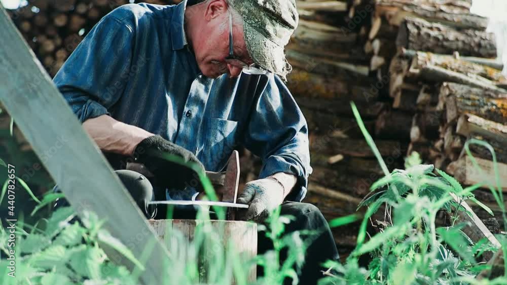 farmer man sharpens the blade of a hand scythe with a hammer. vídeo de ...
