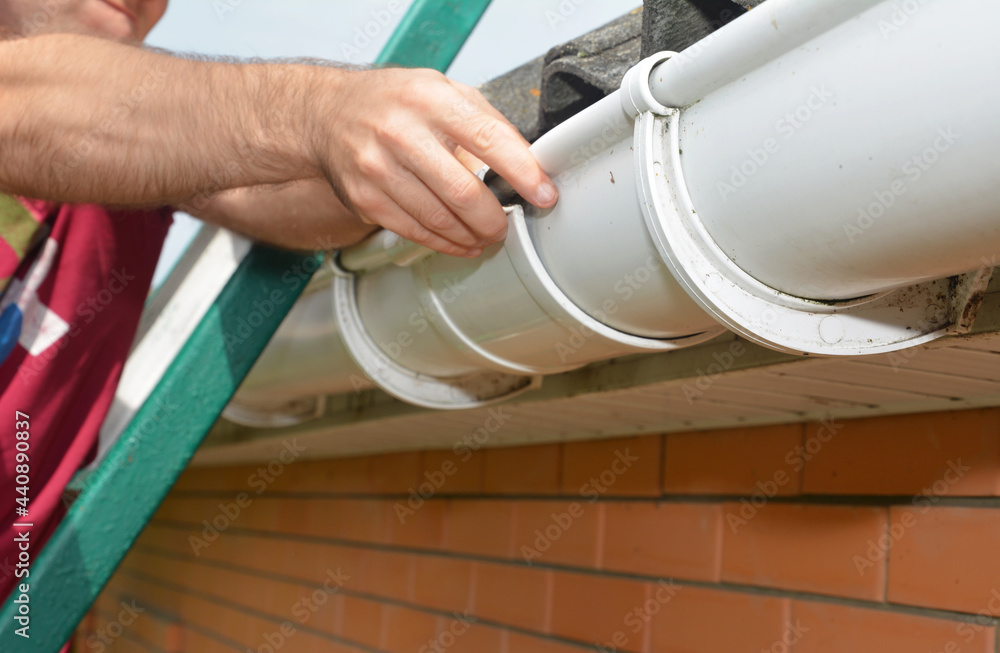 Roof gutter installation. A man on a ladder is installing a roof gutter ...