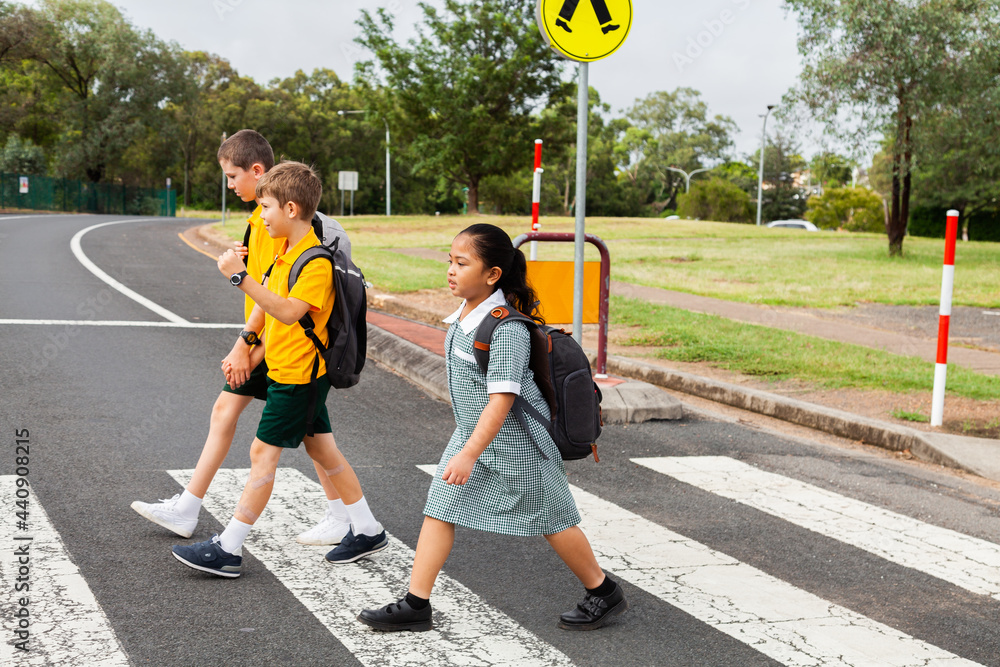 Three public school kids walking to school - crossing the road at a ...