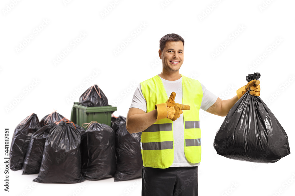 Garbageman holding a plastic bag in front of a bin and a pile of bags ...