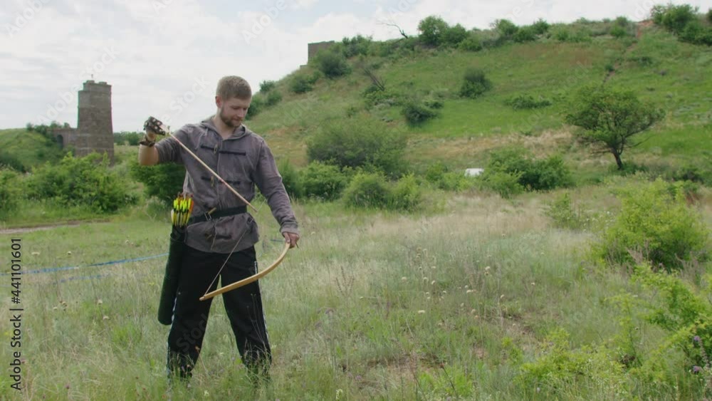 a young guy shoots a bow at a target, in nature, and hits the target ...