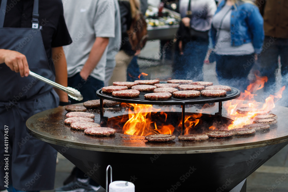 Many burger patties are grilled over an open fire. Street food. Food ...