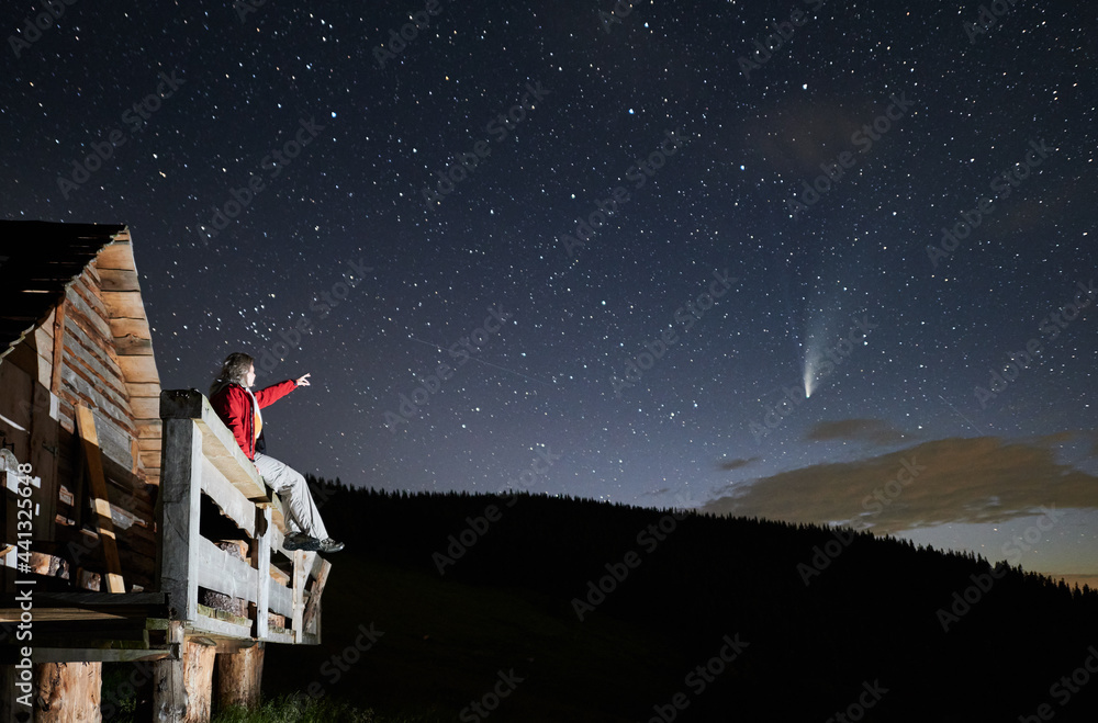 Side view of young man sitting and looking starry sky at home from ...